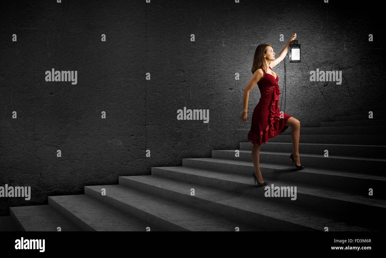 Young attractive woman in red dress with lantern walking in darkness ...