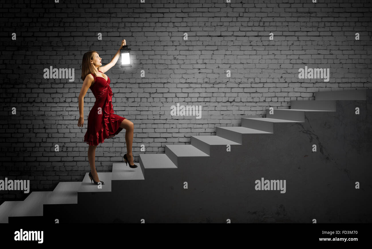 Young attractive woman in red dress with lantern walking in darkness ...