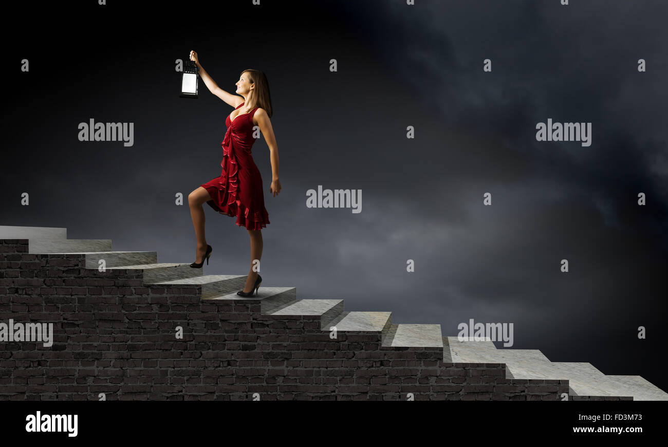 Young attractive woman in red dress with lantern walking in darkness ...