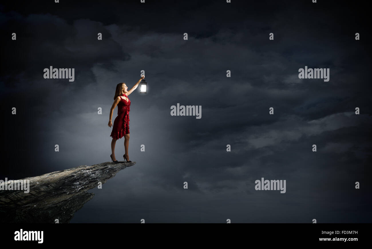 Young attractive woman in red dress with lantern walking in darkness ...