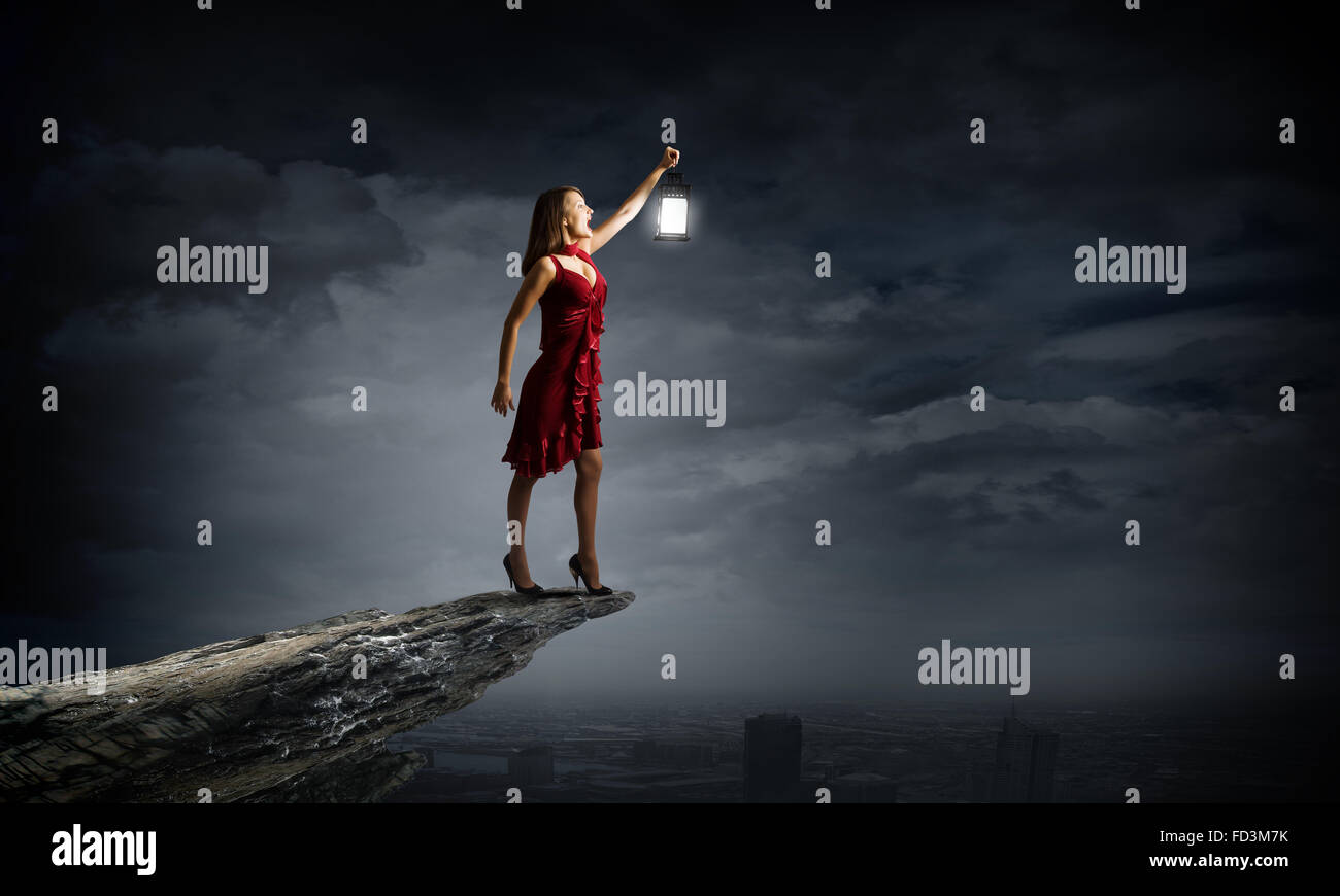 Young attractive woman in red dress with lantern walking in darkness ...