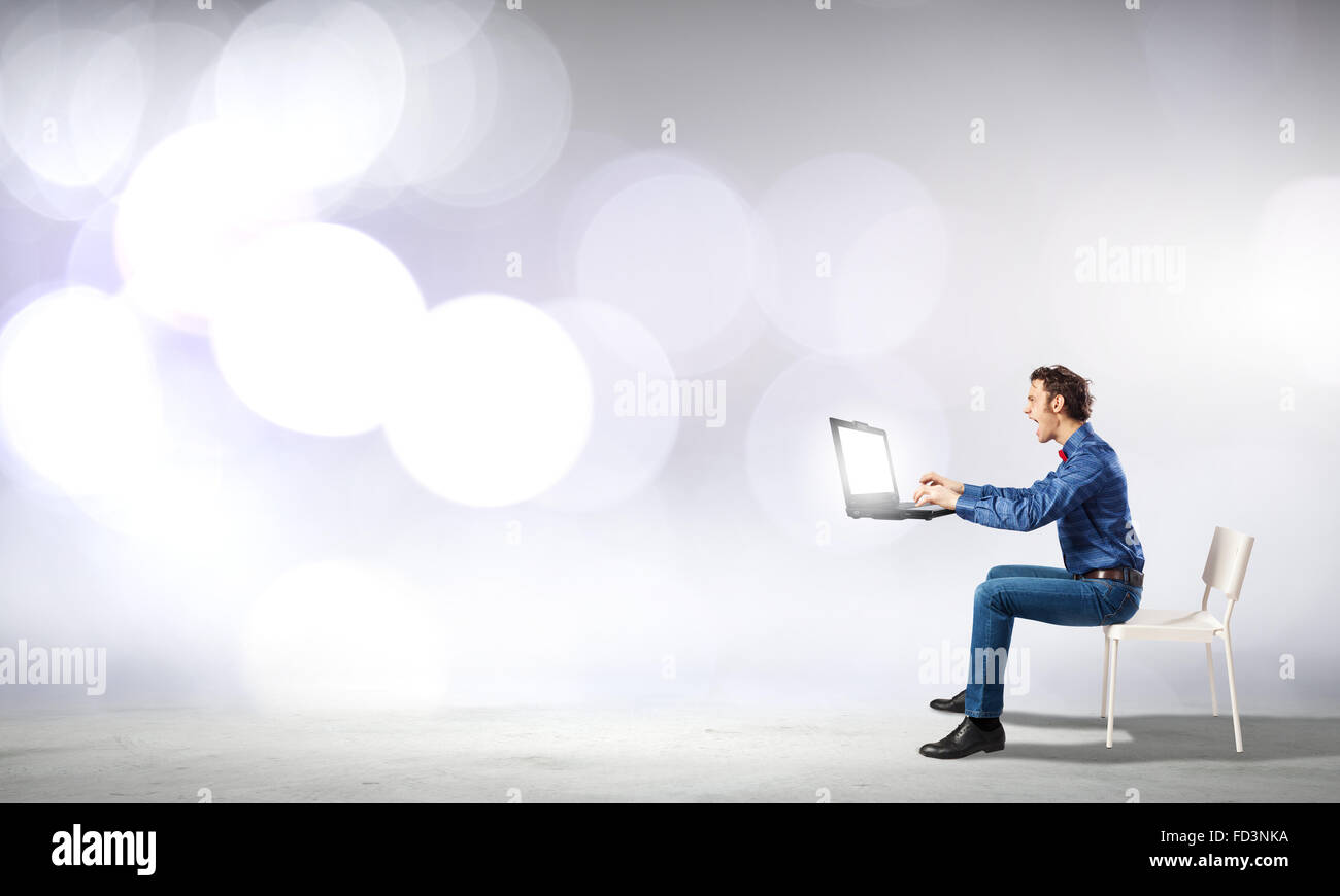 Young man sitting in chair and using laptop Stock Photo - Alamy