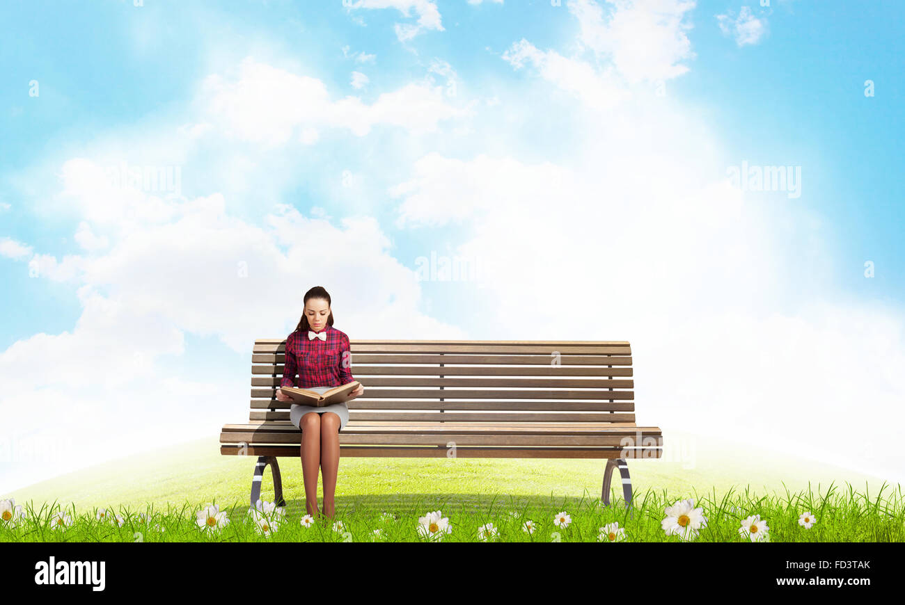 Young woman sitting on bench and reading book Stock Photo - Alamy