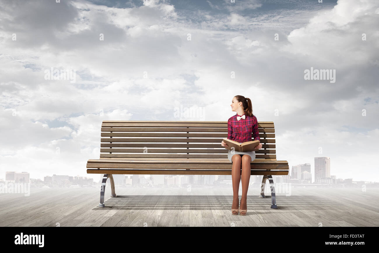 Young woman sitting on bench and reading book Stock Photo - Alamy