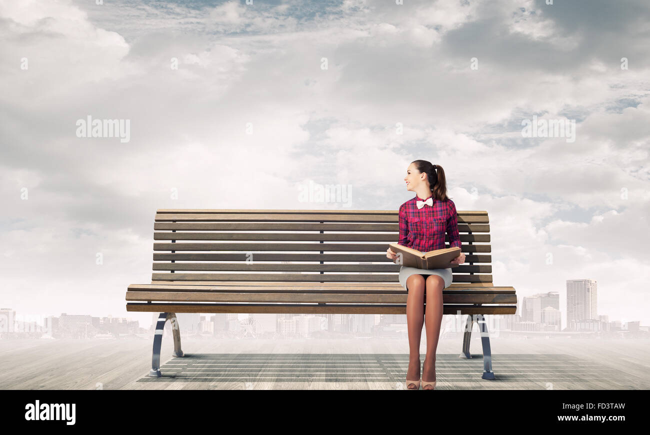 Young woman sitting on bench and reading book Stock Photo - Alamy