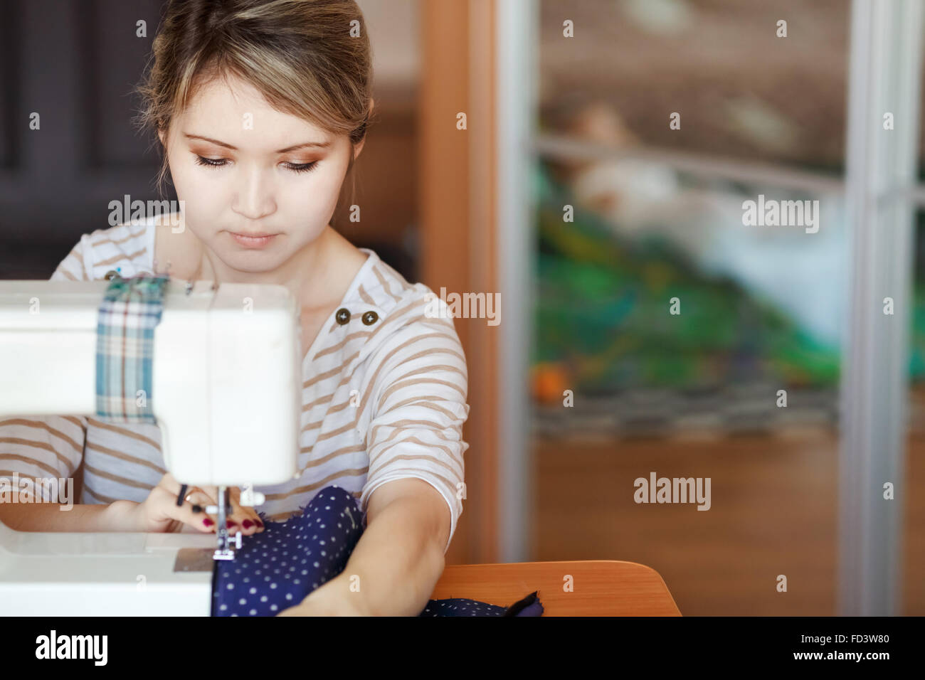 Young woman sewing with sew machine at home while sitting by her ...