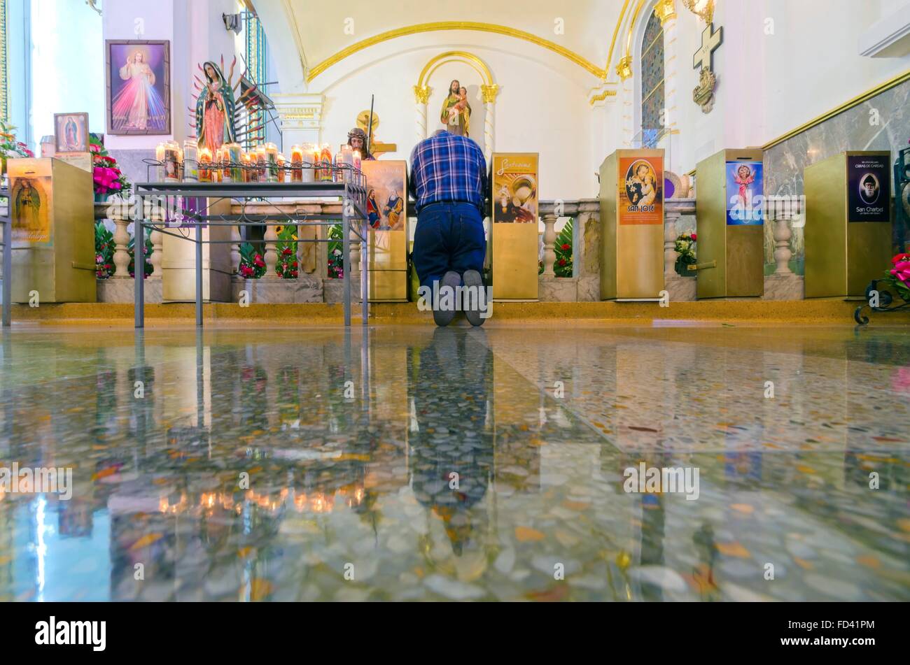 A christian catholic man kneeling and praying on the side altar of ...