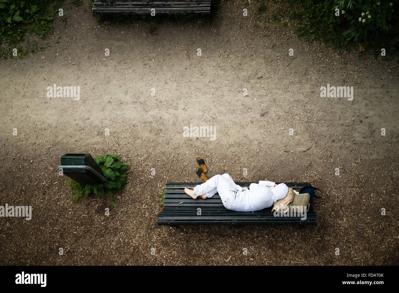 Homeless man dressed clean in white resting on a bench in the park ...