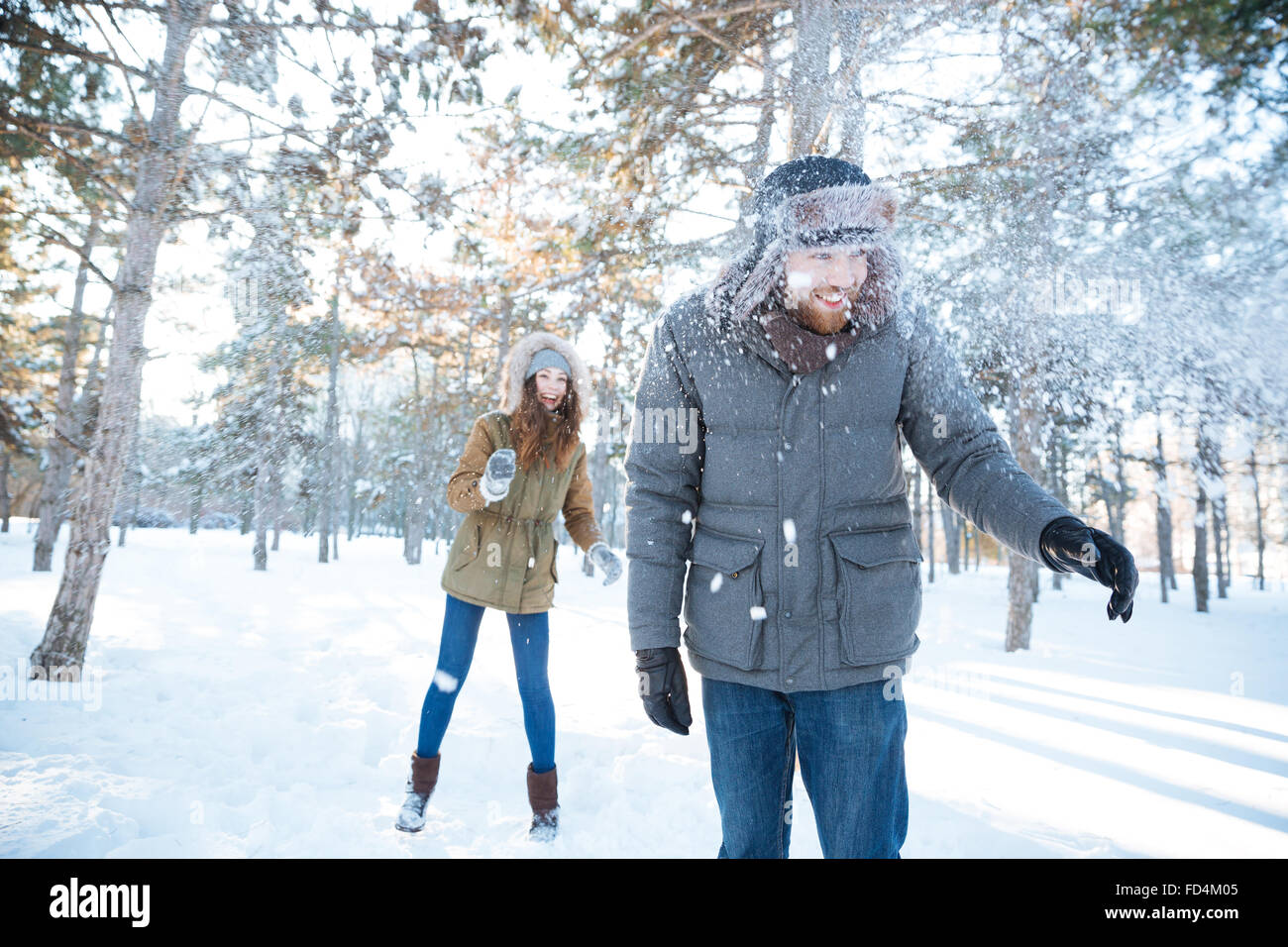 Cheerful young woman playing snowballs with her boyfriend in winter ...