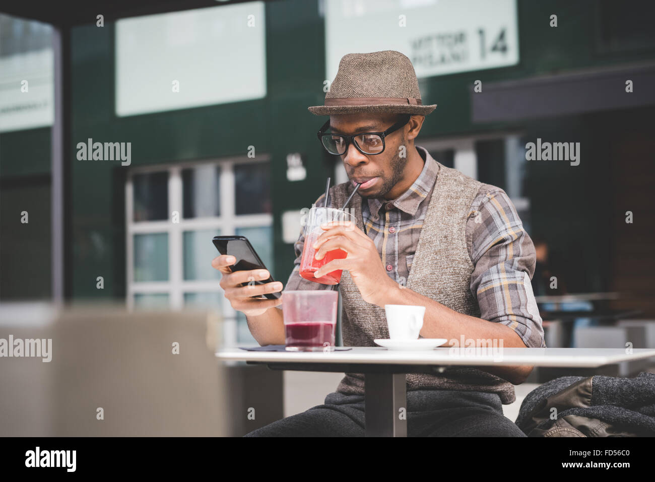 young handsome afro black man sitting on a table, smartphone handhold, looking down the screen ...