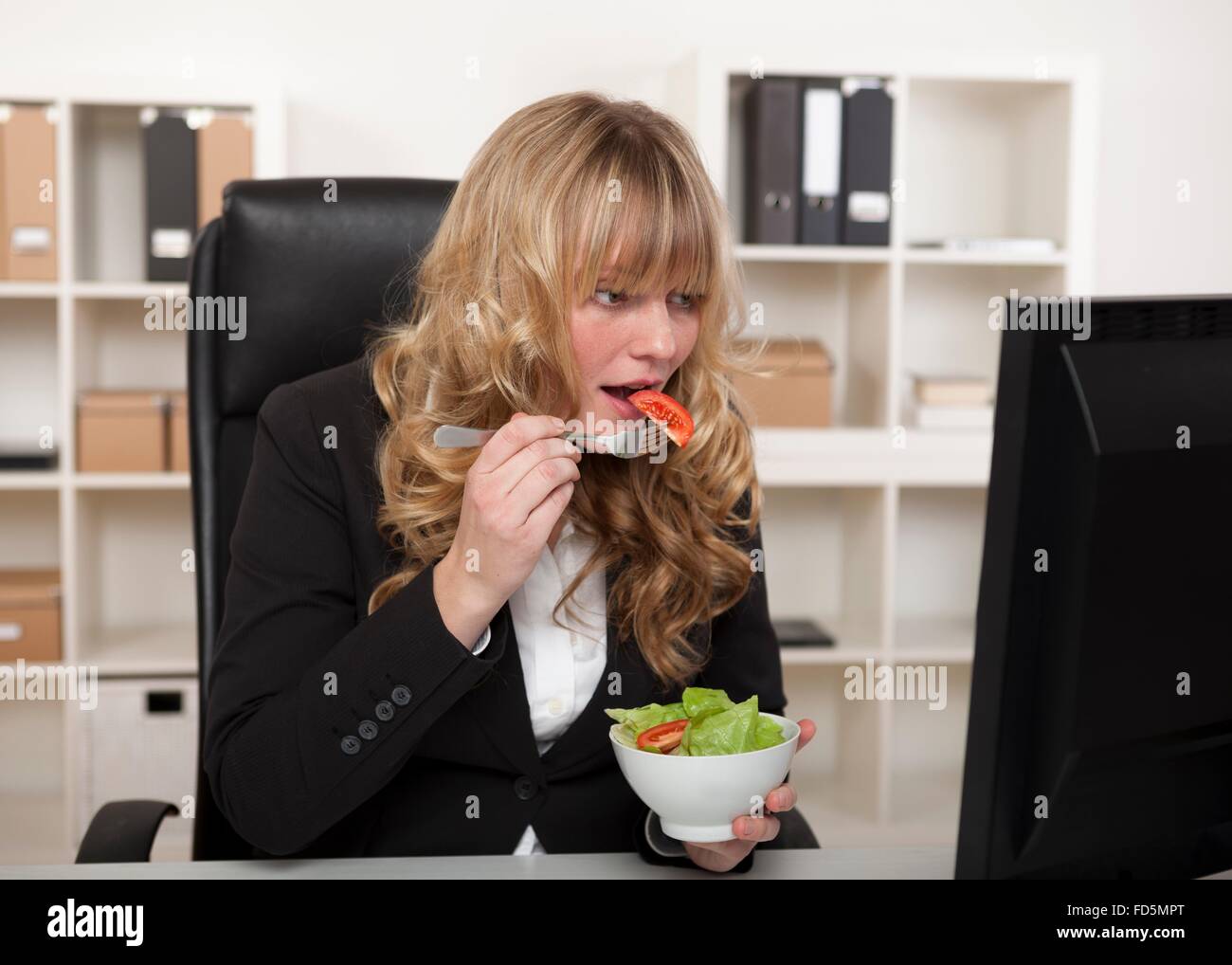 Businesswoman having a quick snack at her desk eating a healthy green ...