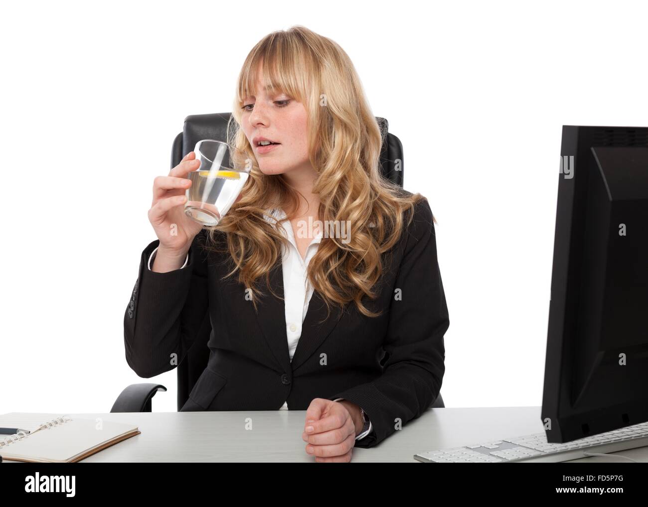 Young businesswoman sitting at her desk drinking a glass of pure ...