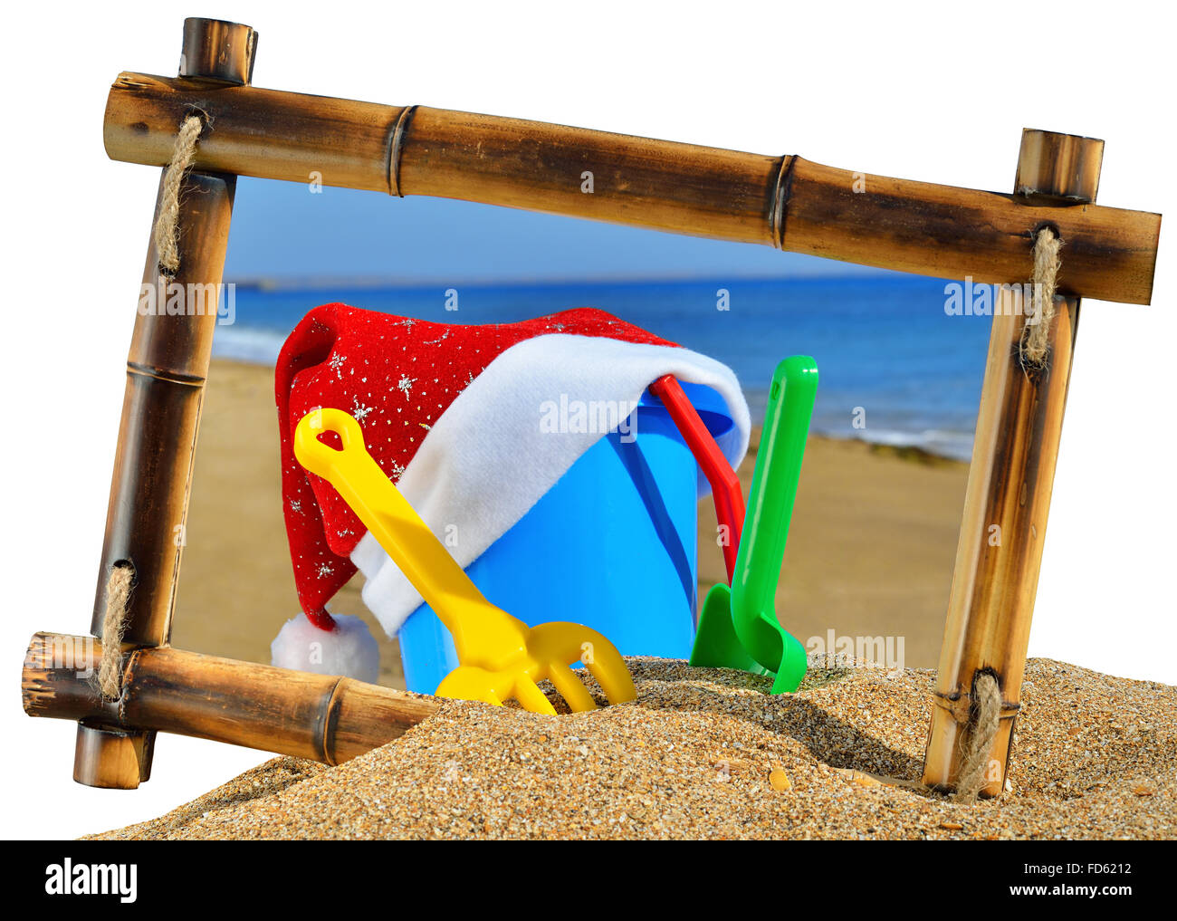 Baby toys and Santa's hat in bamboo frame on the beach against a blue ...