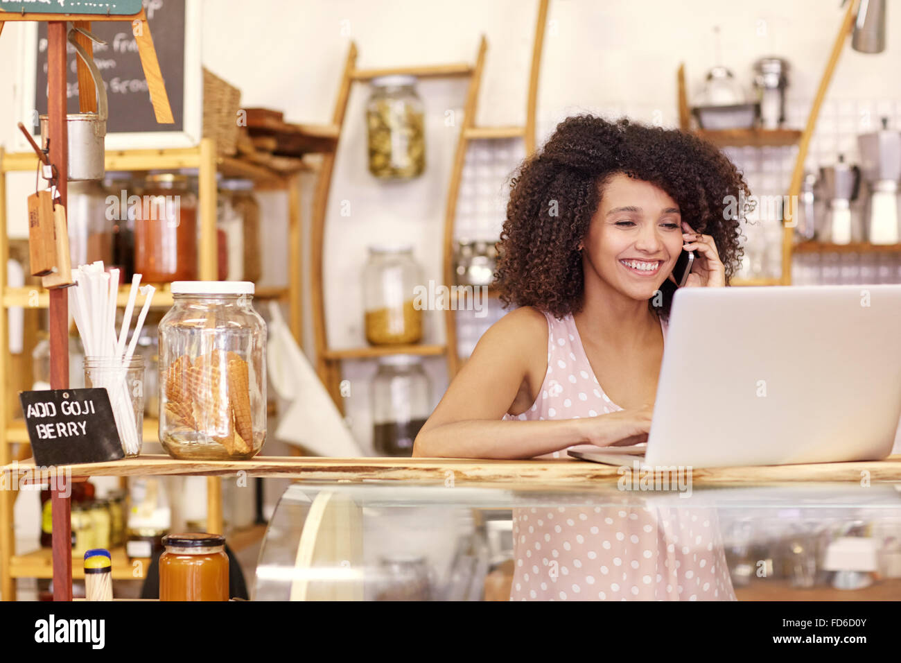 Smiling coffee shop owner typing on a laptop while talking Stock Photo ...