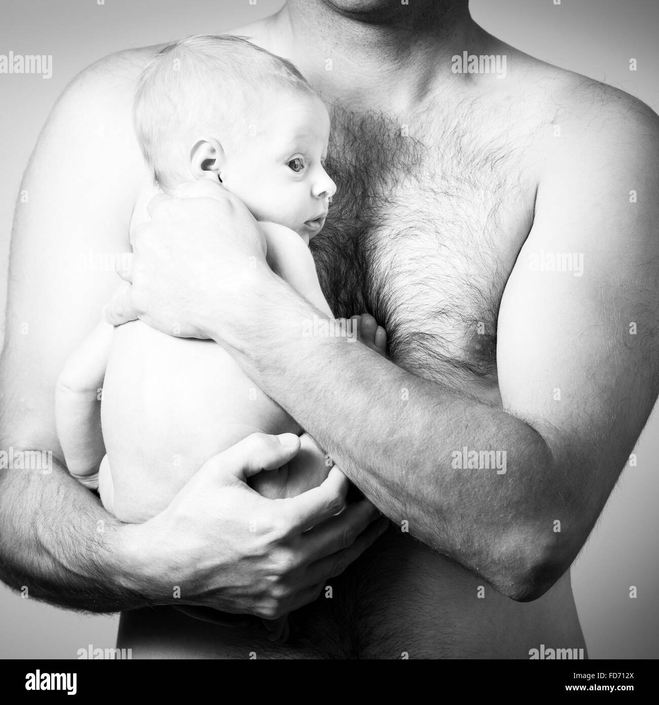 Cute newborn baby boy being held in his dad's arms against a bare chest ...