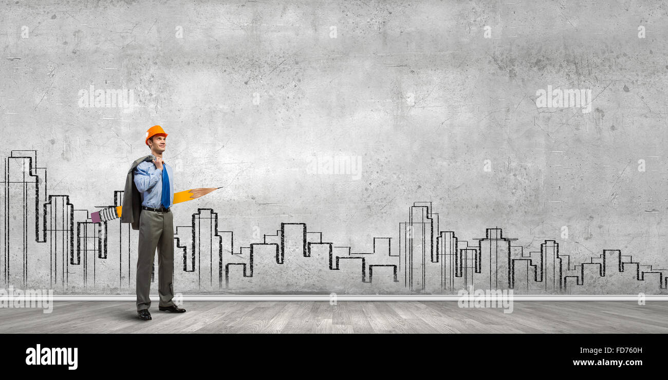 Young man engineer with huge pencil in hands and construction sketches ...