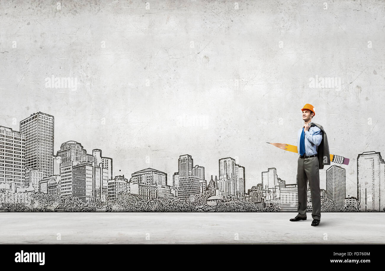 Young man engineer with huge pencil in hands and construction sketches ...