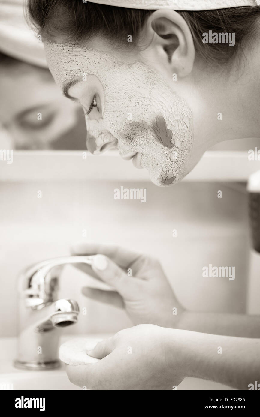 Woman removing facial dried clay mud mask with sponge in bathroom in ...