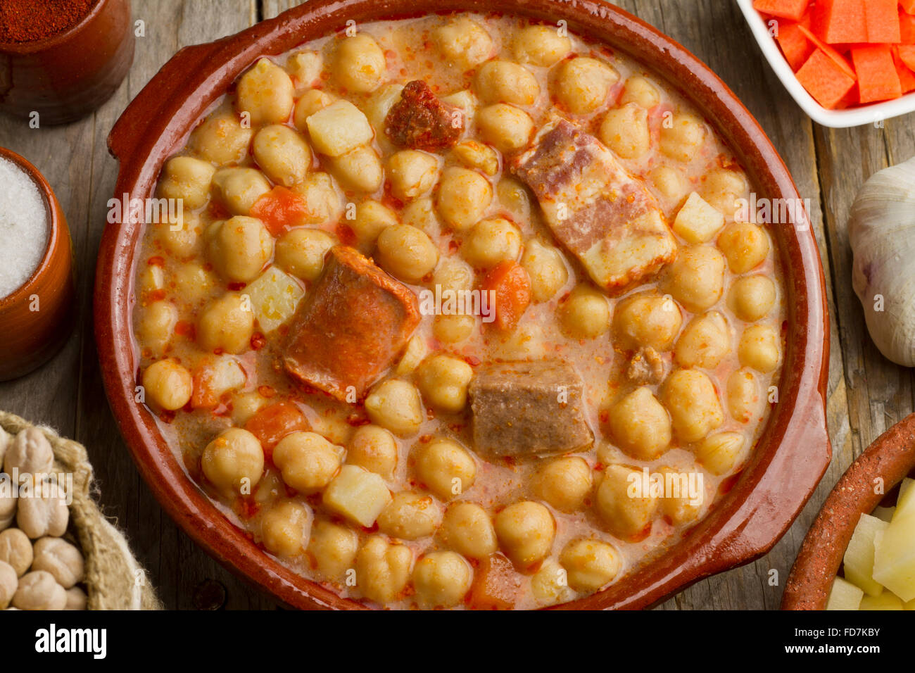 Spanish Cocido in an earthenware pot and admixtures on bowls on a ...