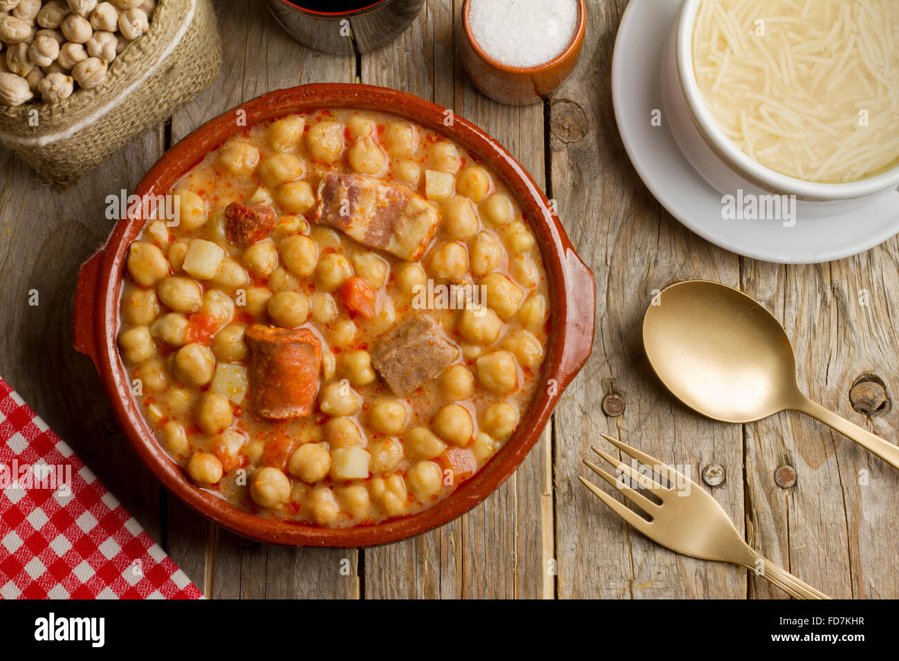 Spanish Cocido in an earthenware pot and soup in a white bowl on a ...