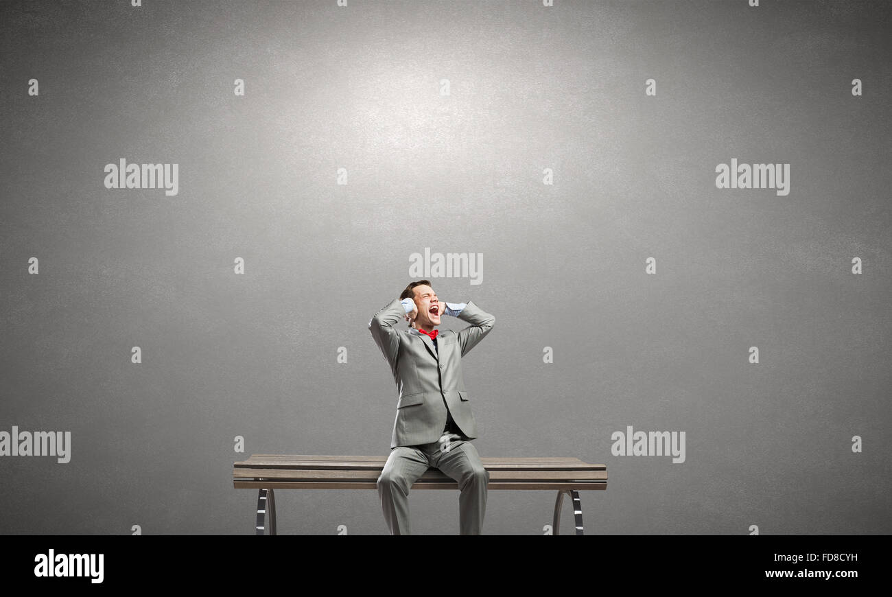 Frustrated businessman sitting on bench closing his ears and screaming ...