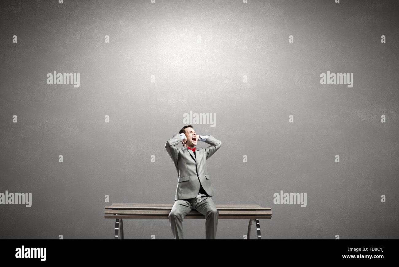 Frustrated businessman sitting on bench closing his ears and screaming ...