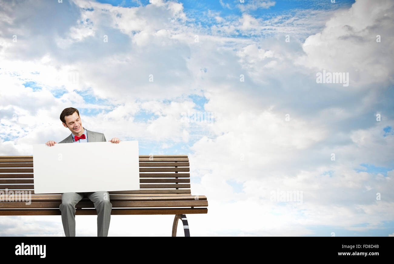 Young man sitting on bench with white banner Stock Photo - Alamy