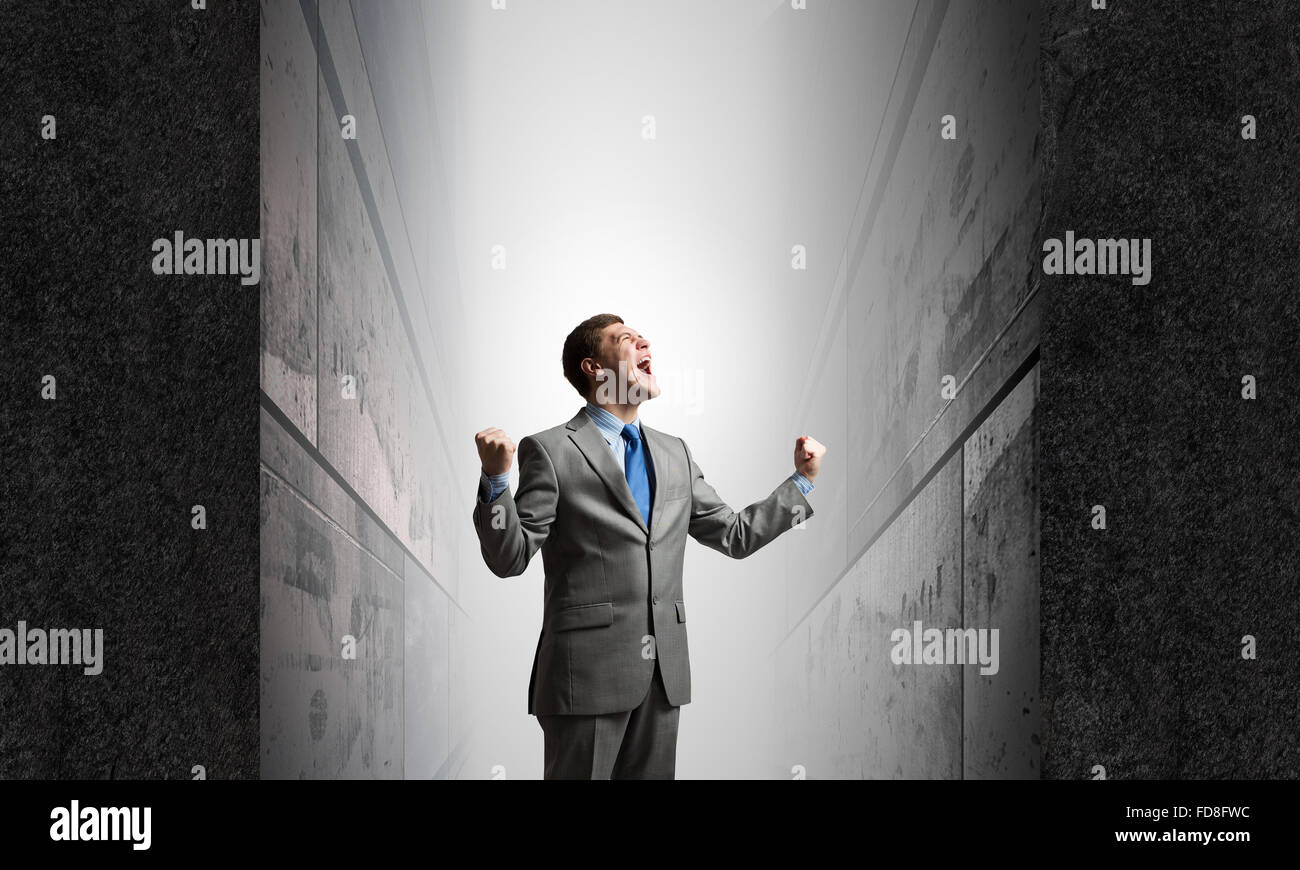 Young confident businessman with hands up screaming emotionally above ...