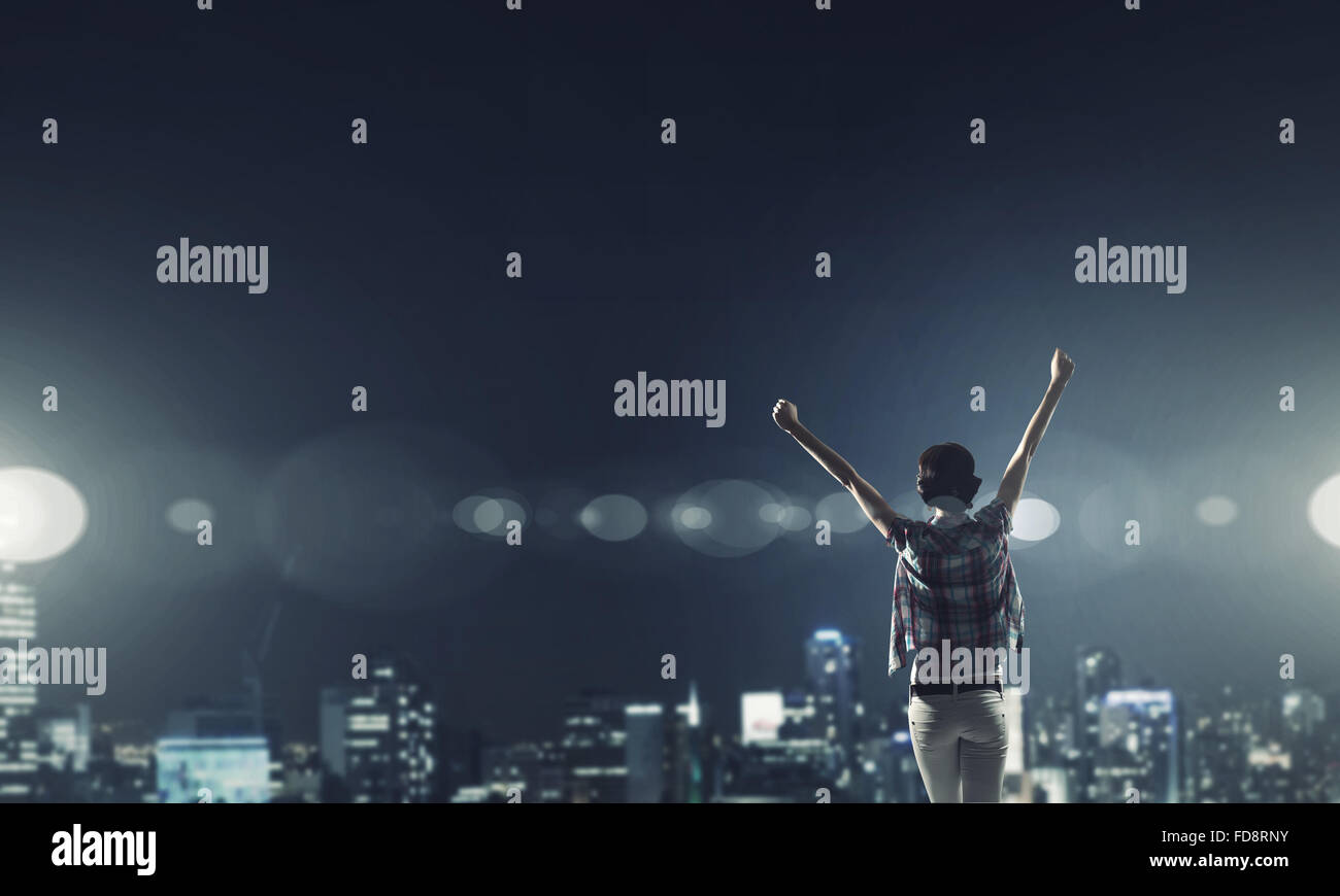 Rear view of young woman with hands up looking at night city Stock ...