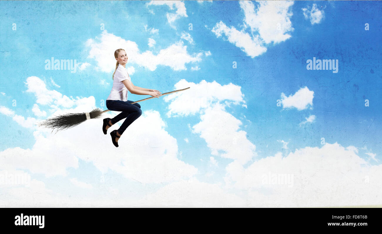 Young girl in casual flying on broom high in sky Stock Photo - Alamy