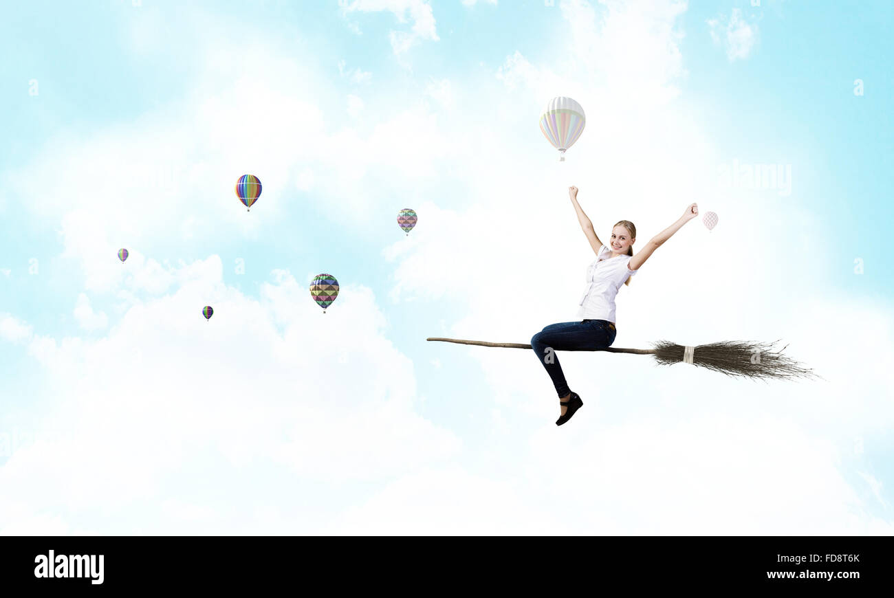Young girl in casual flying on broom high in sky Stock Photo - Alamy