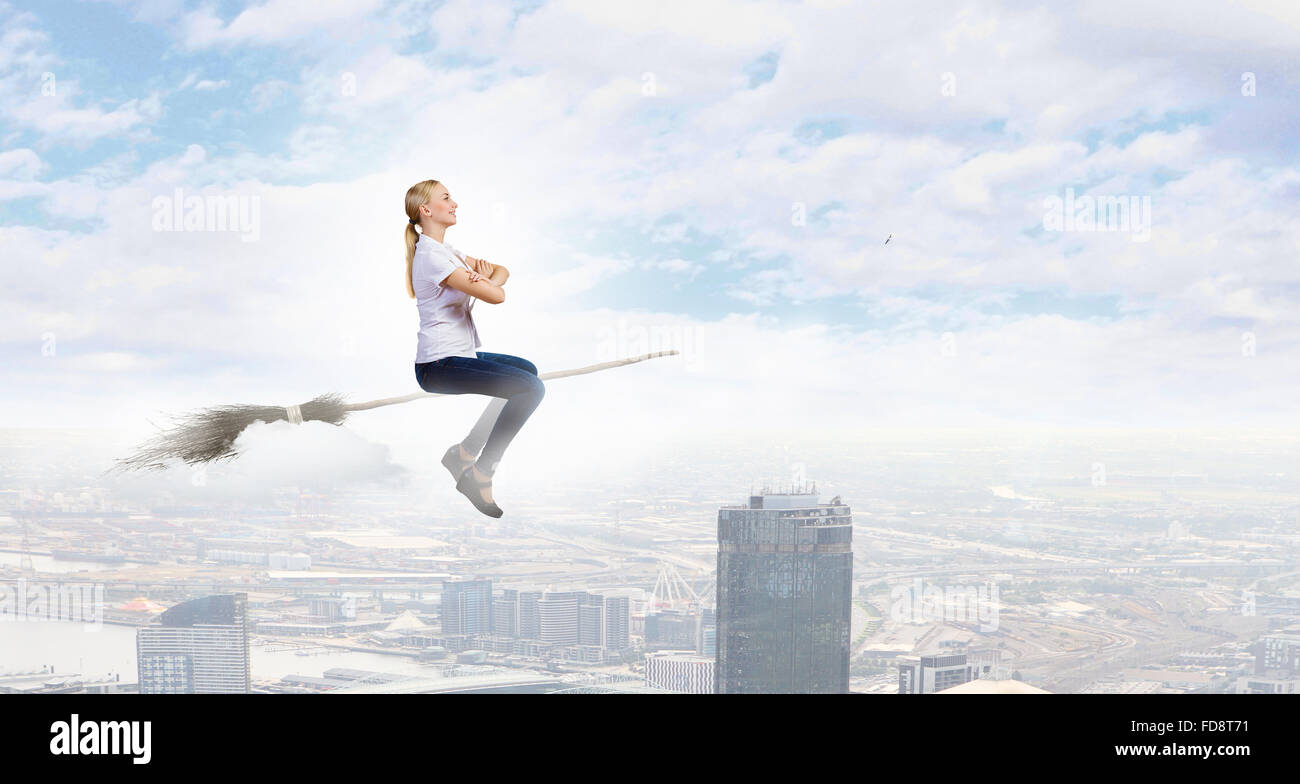 Young girl in casual flying on broom high in sky Stock Photo - Alamy