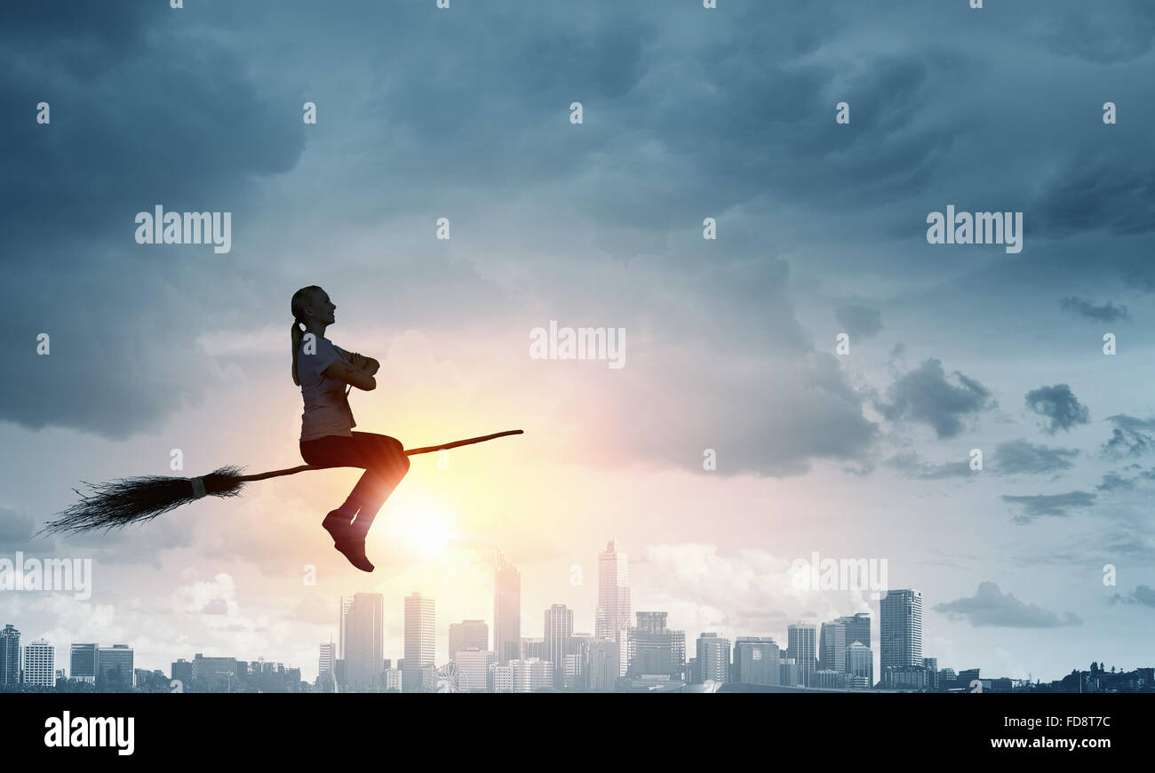 Young girl in casual flying on broom high in sky Stock Photo - Alamy