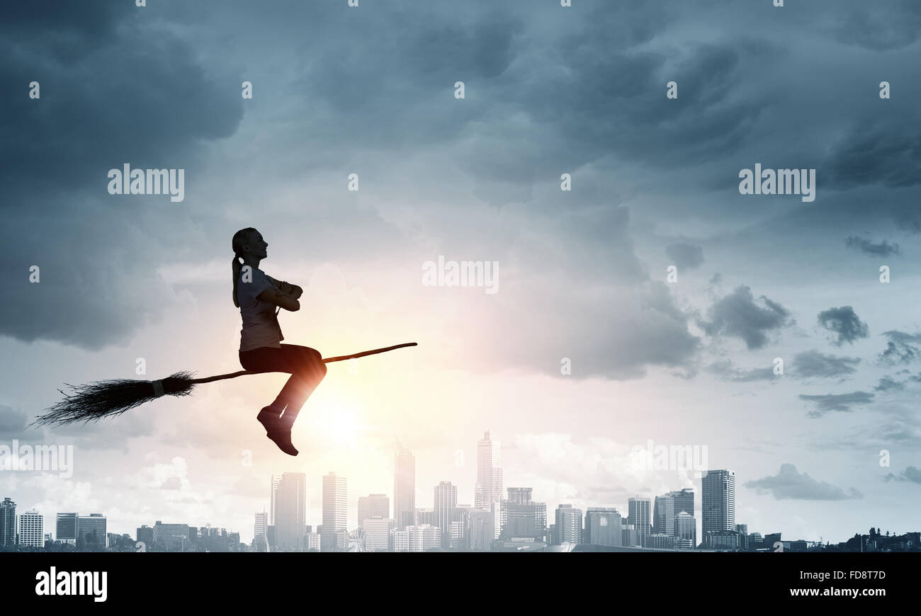 Young girl in casual flying on broom high in sky Stock Photo - Alamy