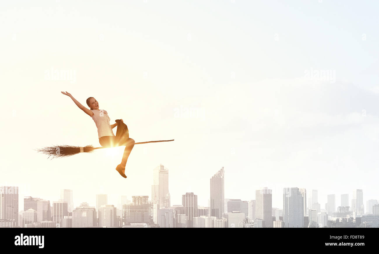 Young girl in casual flying on broom high in sky Stock Photo - Alamy