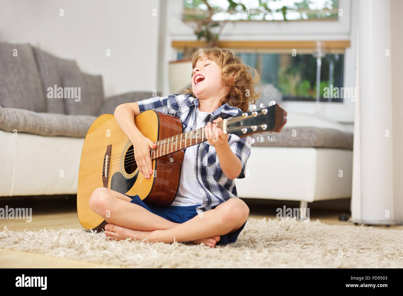 Happy boy singing and playing the guitar at home Stock Photo - Alamy
