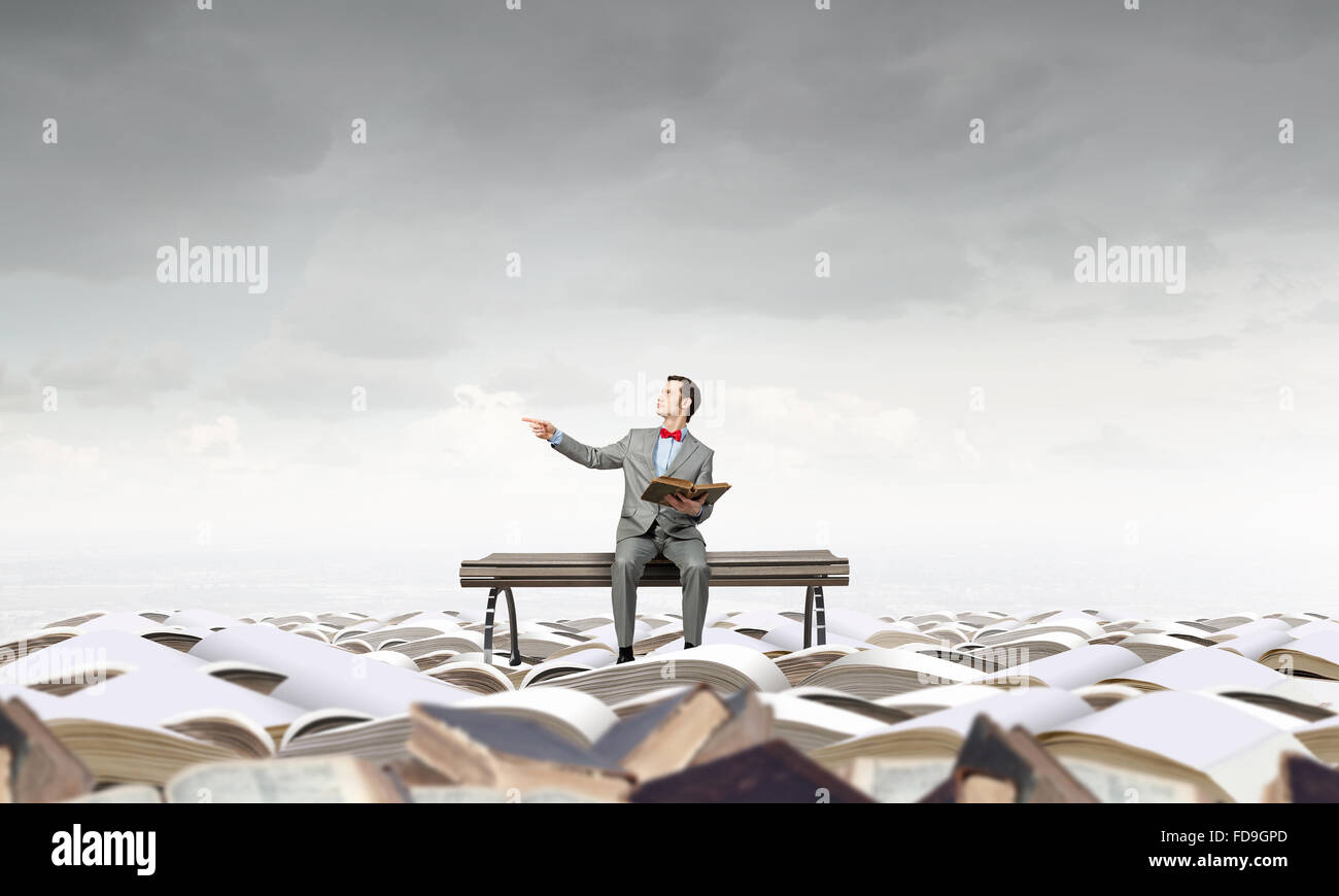 Young businessman sitting on bench with book in hands and pointing with ...
