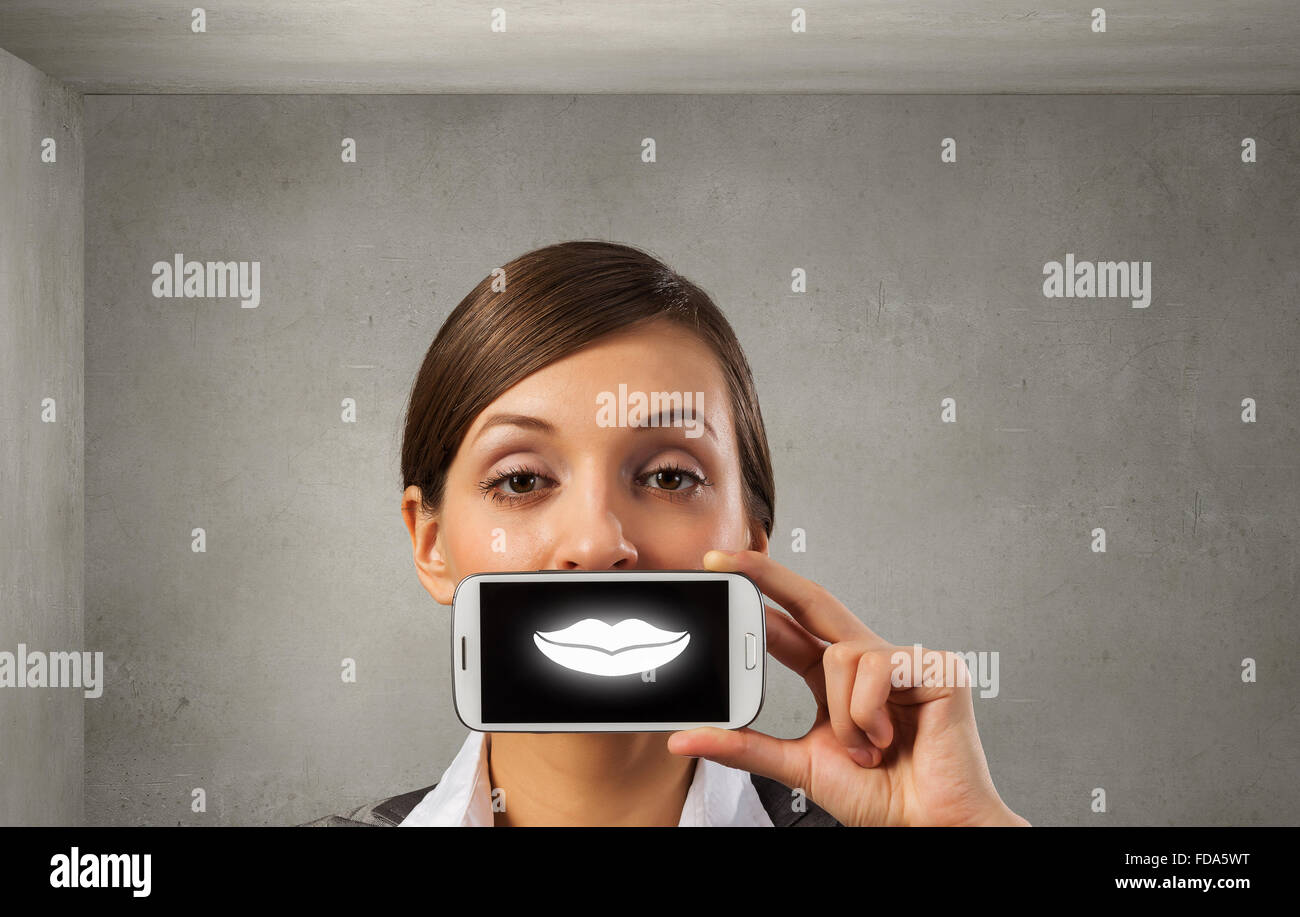 Beautiful young woman holding mobile phone against her mouth and ...