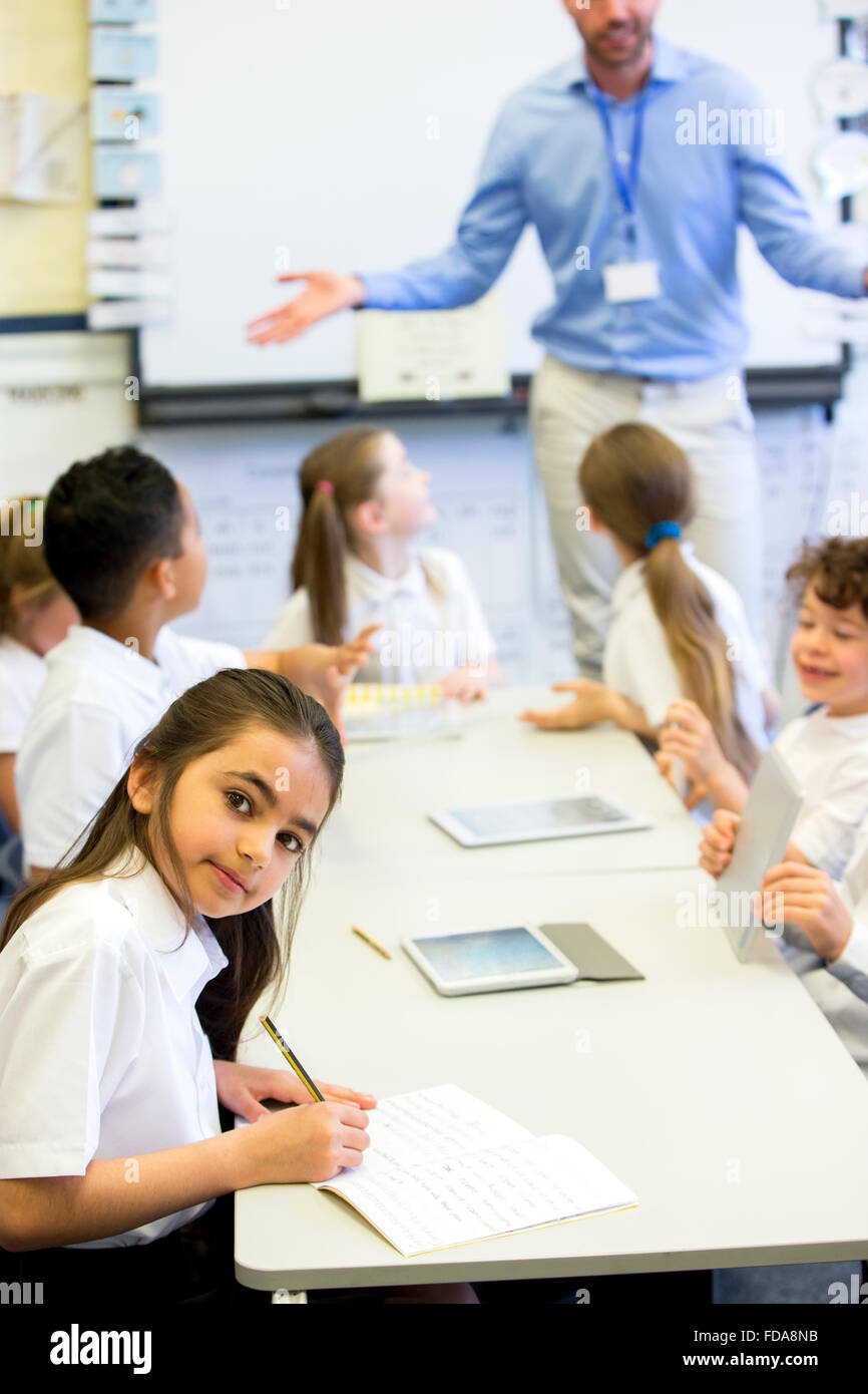 School girl smiles at the camera as she sits at her desk while working ...