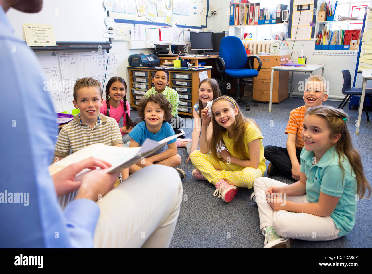 A group of children sit on the floor cross legged, listening to the ...