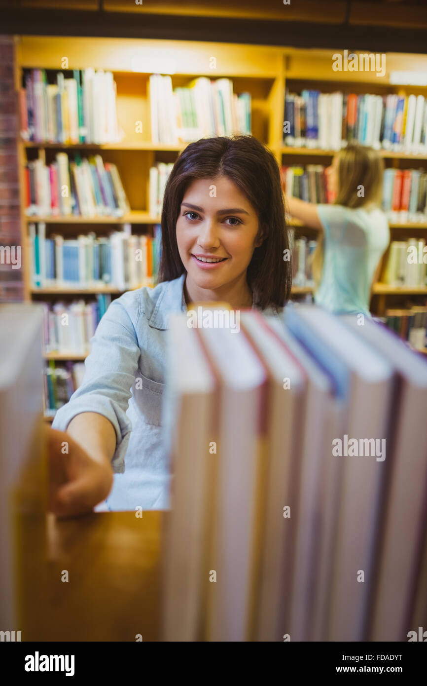 Smiling brunette picking out a book of bookshelves Stock Photo - Alamy