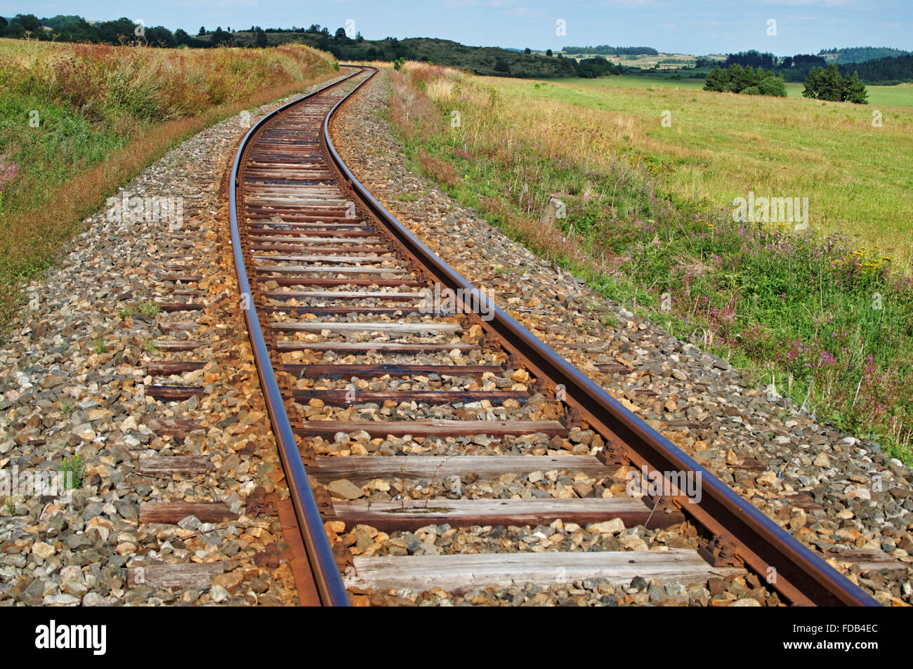 Rusty railroad tracks on a railway embankment between meadows, hills in ...