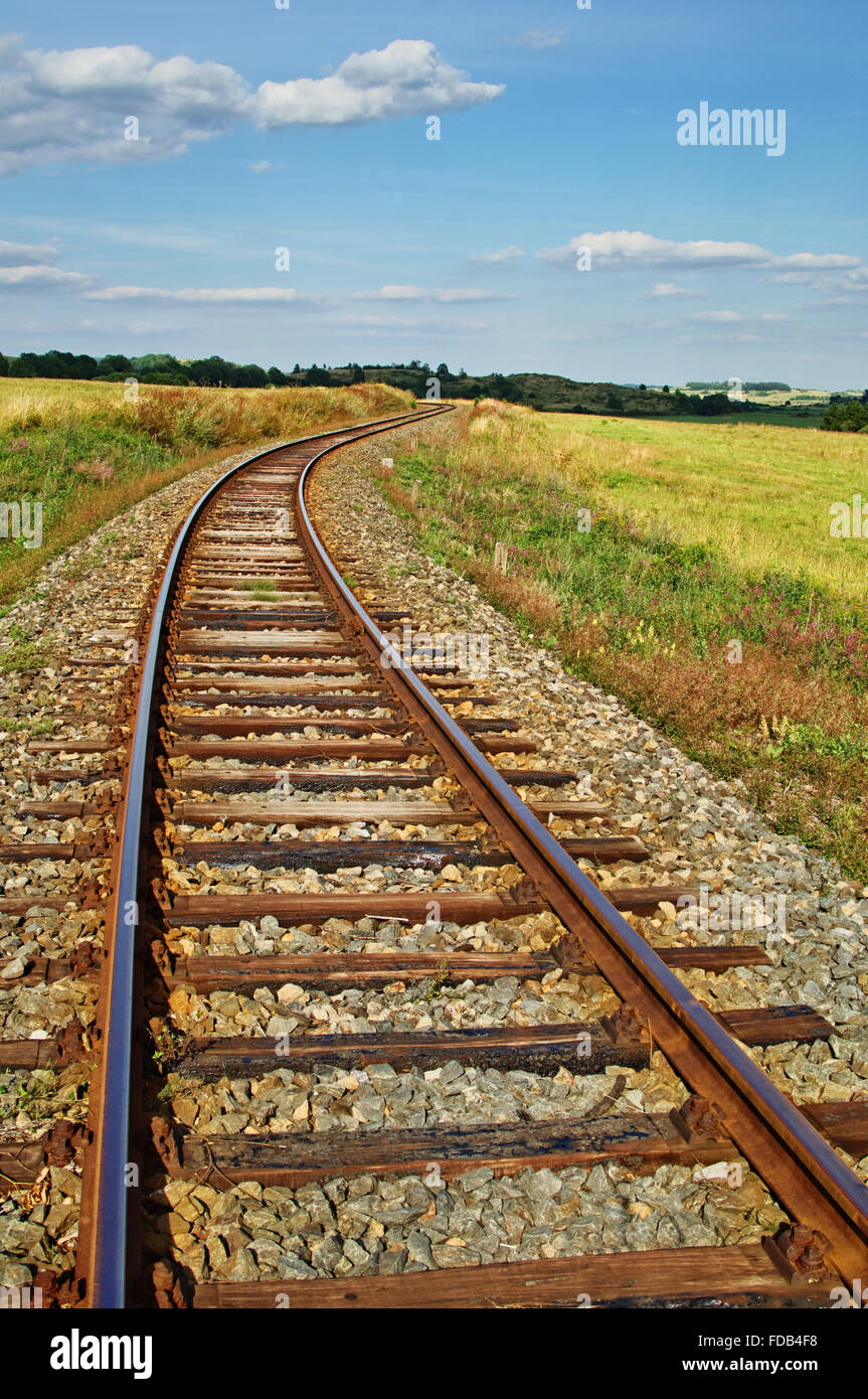 Rusty railroad tracks on a railway embankment between meadows, hills in ...