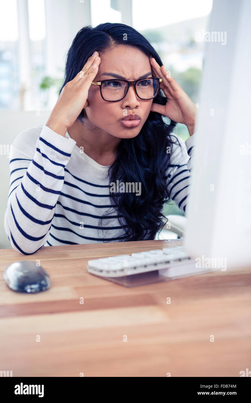 Frowning Asian woman looking at computer monitor with hands on head ...