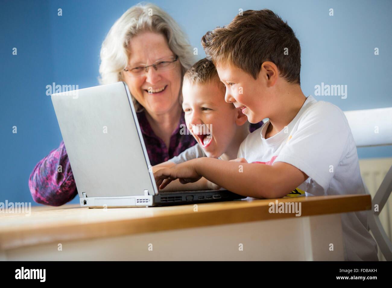 MODEL RELEASED. Two boys using a laptop computer with their grandmother ...