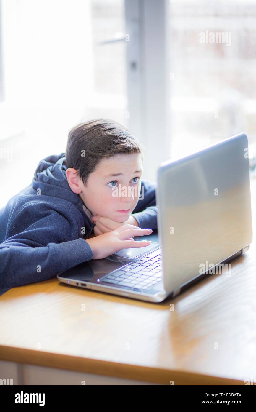 MODEL RELEASED. Boy using a laptop computer with his hand on his chin ...