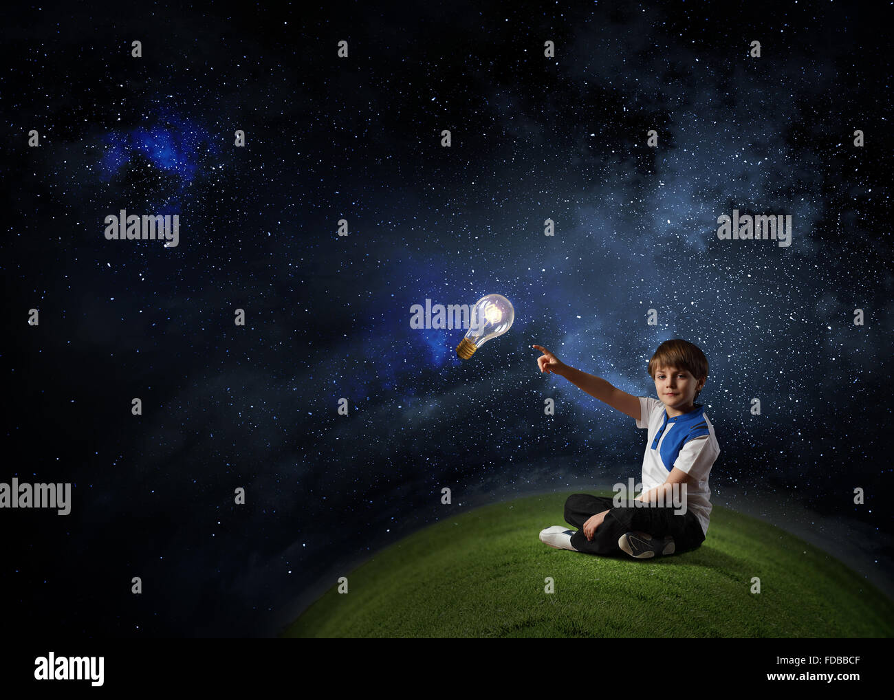Cute school boy sitting on grass and touching glass light bulb with ...