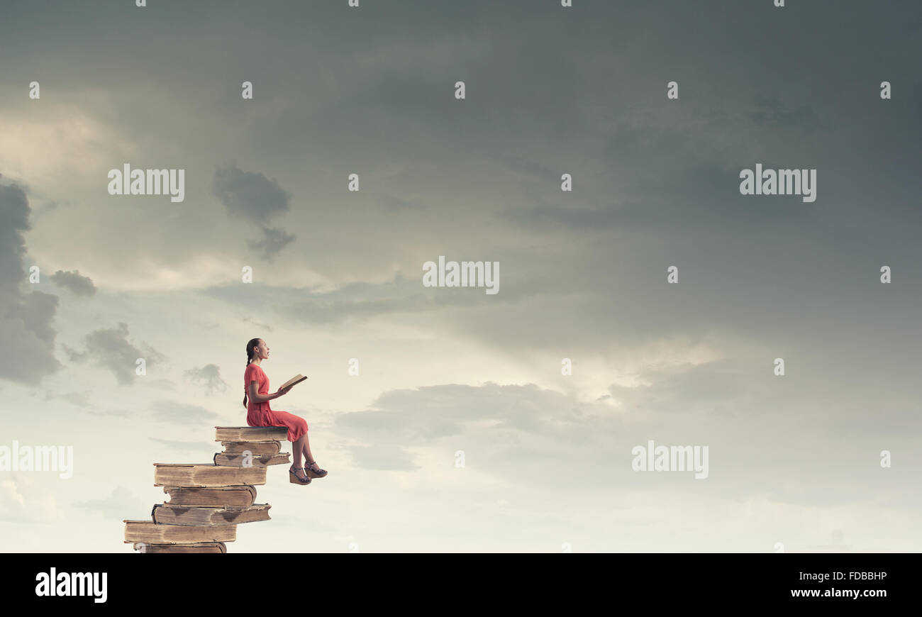 Young girl sitting on stack of books and reading Stock Photo - Alamy