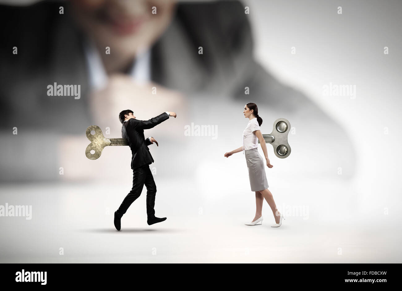 Young businessman and businesswoman walking with wind up key in his ...