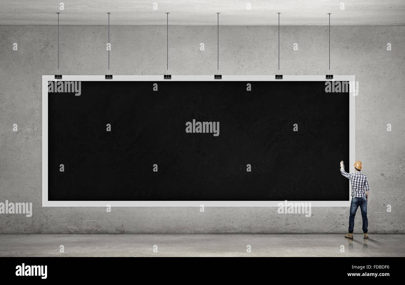 Rear view of man engineer in helmet drawing on chalkboard Stock Photo ...